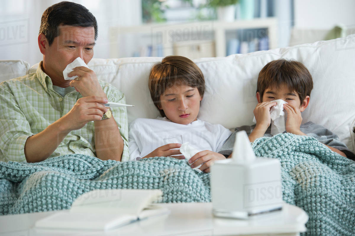 Sick father and sons blowing noses and checking temperature on living ...
