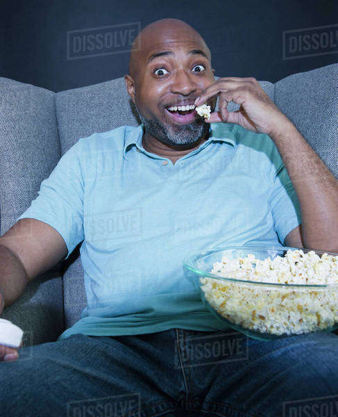 African American man eating popcorn and watching television - Royalty ...