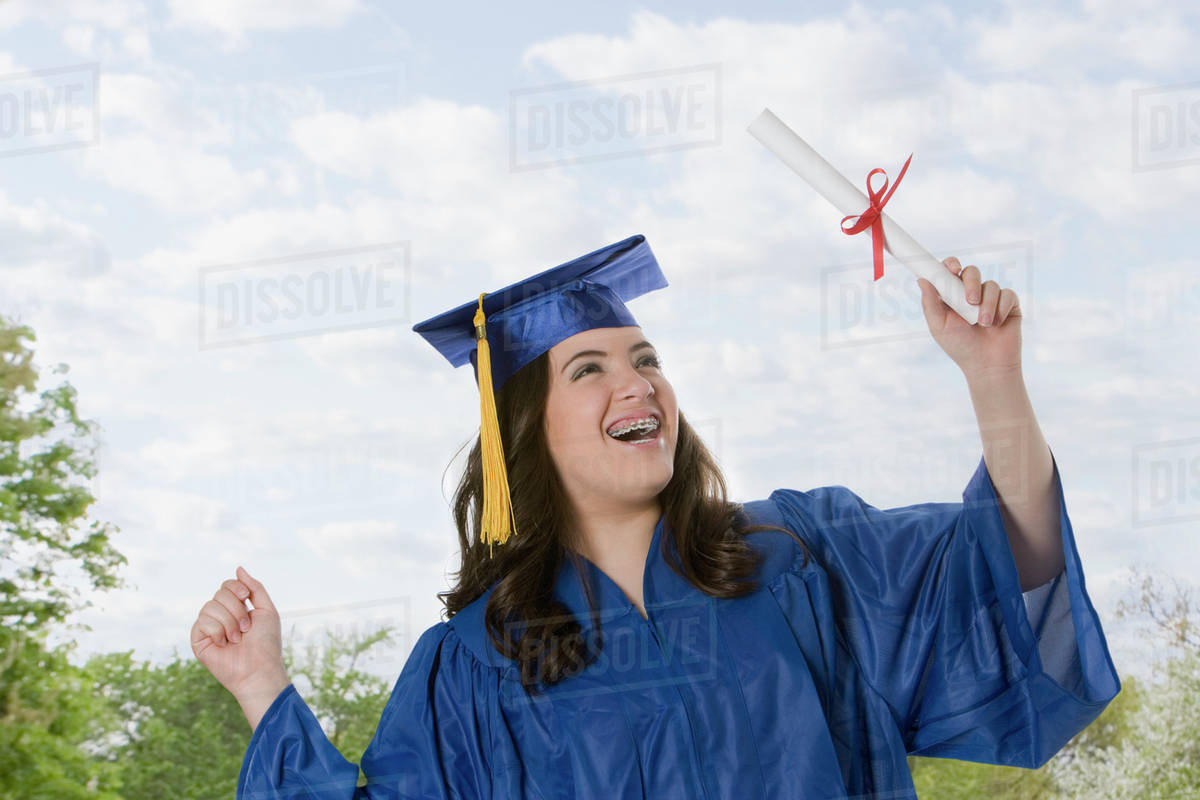 Hispanic teenage girl in graduation cap and gown holding diploma ...