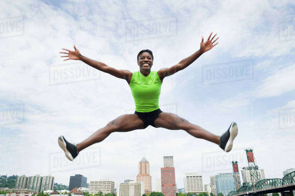 African woman jumping with city in background - Stock Photo - Dissolve