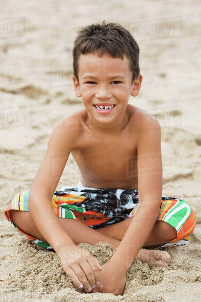 Mixed race boy in swim trunks sitting on beach - Royalty-free Stock ...