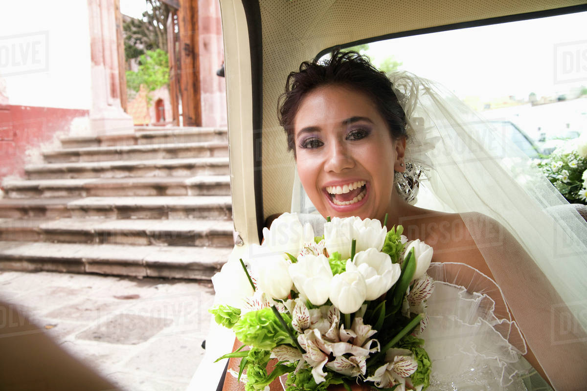 Hispanic bride sitting with bouquet in back of car - Stock Photo - Dissolve