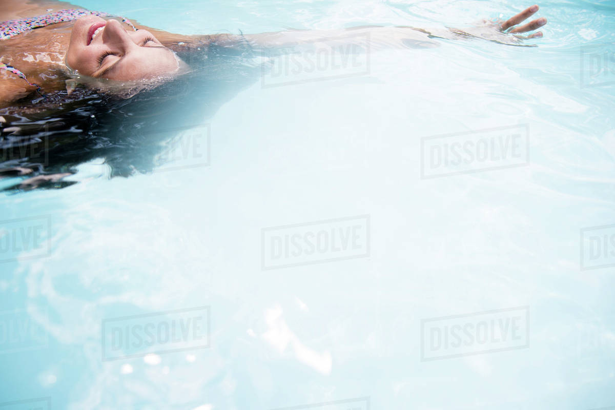 Caucasian woman floating in swimming pool - Stock Photo - Dissolve