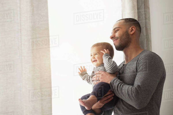 Smiling father and baby son looking out window - Stock Photo - Dissolve