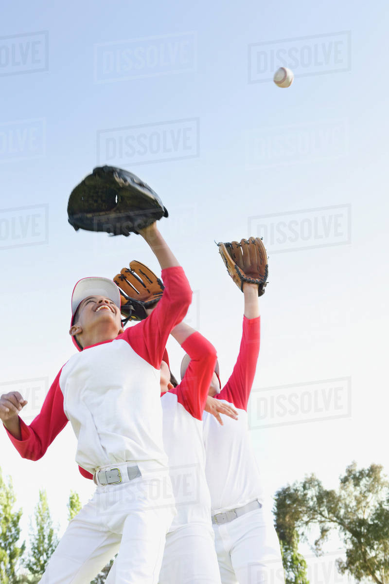 Multi-ethnic boys in baseball uniforms jumping to catch baseball ...