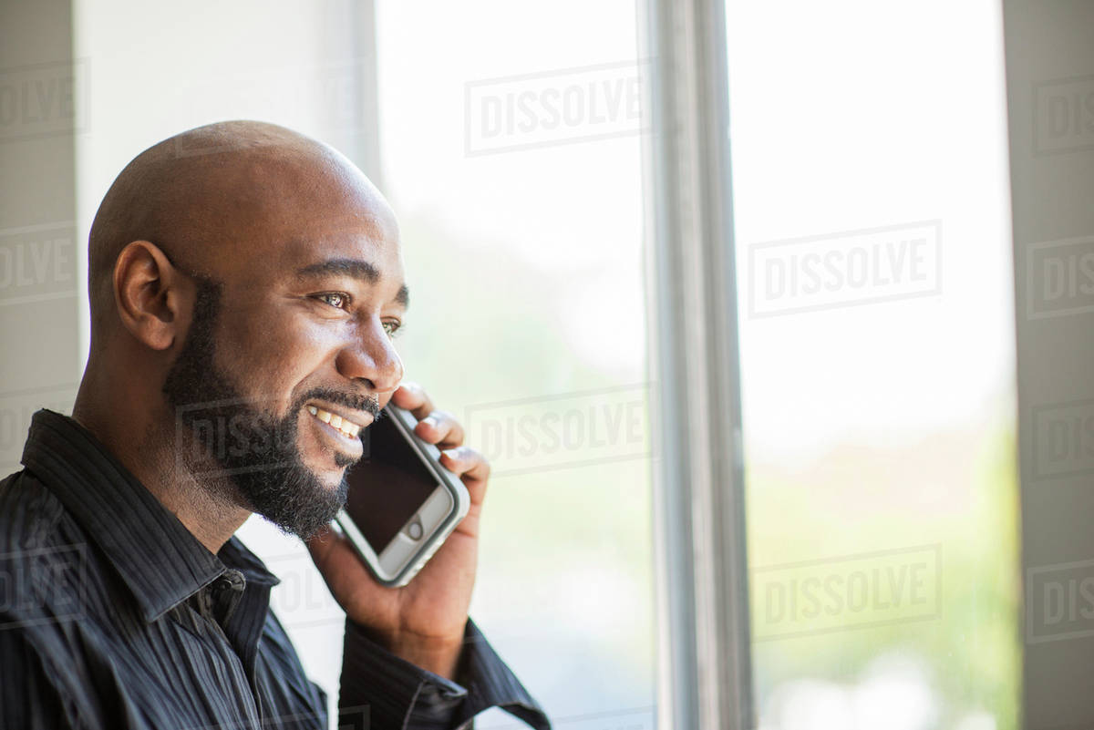Black man talking on cell phone near window - Royalty-free Stock Photo ...