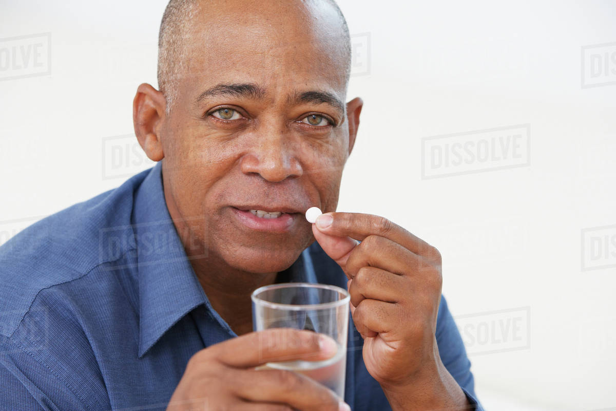 Senior African man taking medication with glass of water - Royalty-free ...