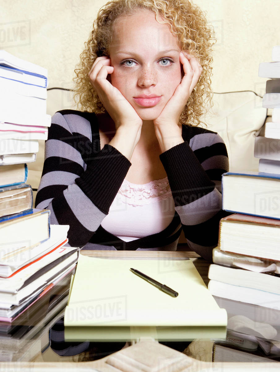 Young woman studying at desk with large stacks of books and notepad ...