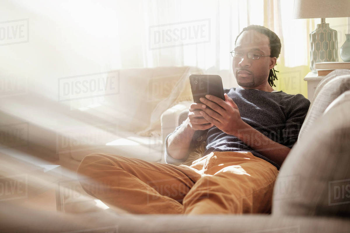 Black man using digital tablet on sofa - Stock Photo - Dissolve
