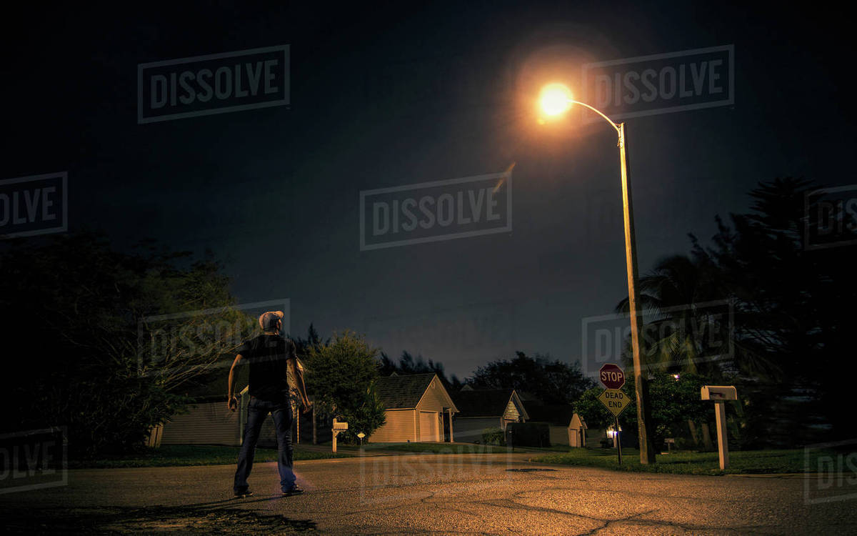 Caucasian man looking up at street light in suburb at night - Royalty ...