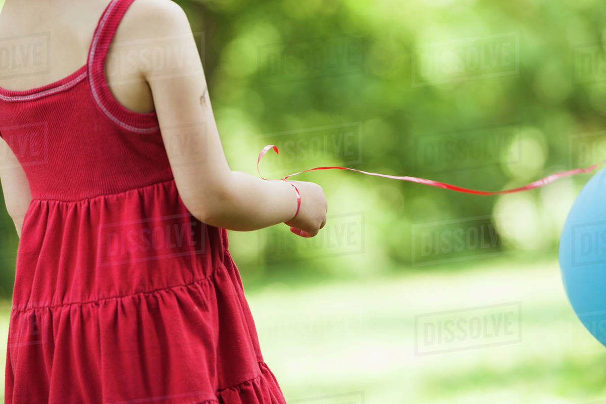Girl with balloon tied to wrist outdoors - Stock Photo - Dissolve