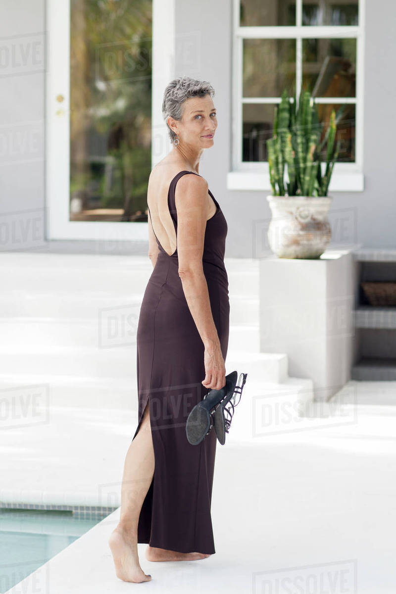 Woman in evening gown carrying shoes by swimming pool - Stock Photo ...