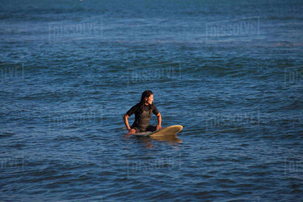 Hispanic surfer floating on surfboard in ocean - Stock Photo - Dissolve
