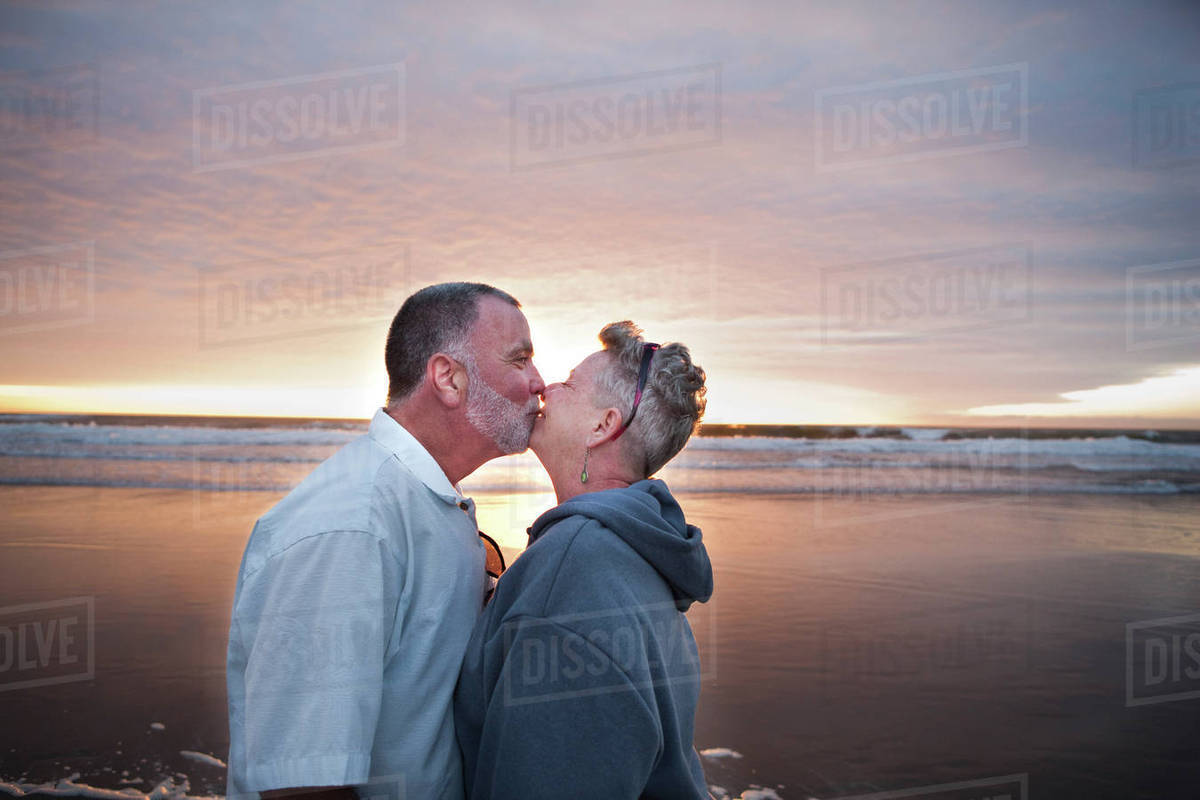 Caucasian couple kissing on beach at sunset - Stock Photo - Dissolve