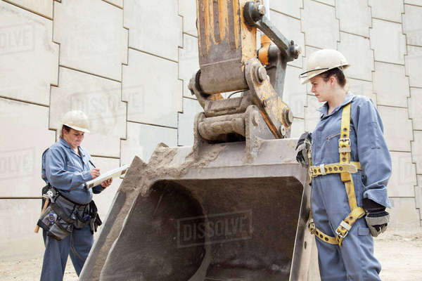 Workers examining digger machinery at construction site - Stock Photo ...