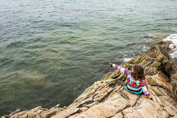 Caucasian girl sitting on rocks pointing at ocean - Royalty-free Stock ...
