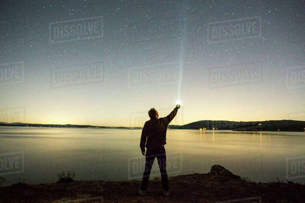 Caucasian man pointing flashlight at night sky near water - Royalty ...