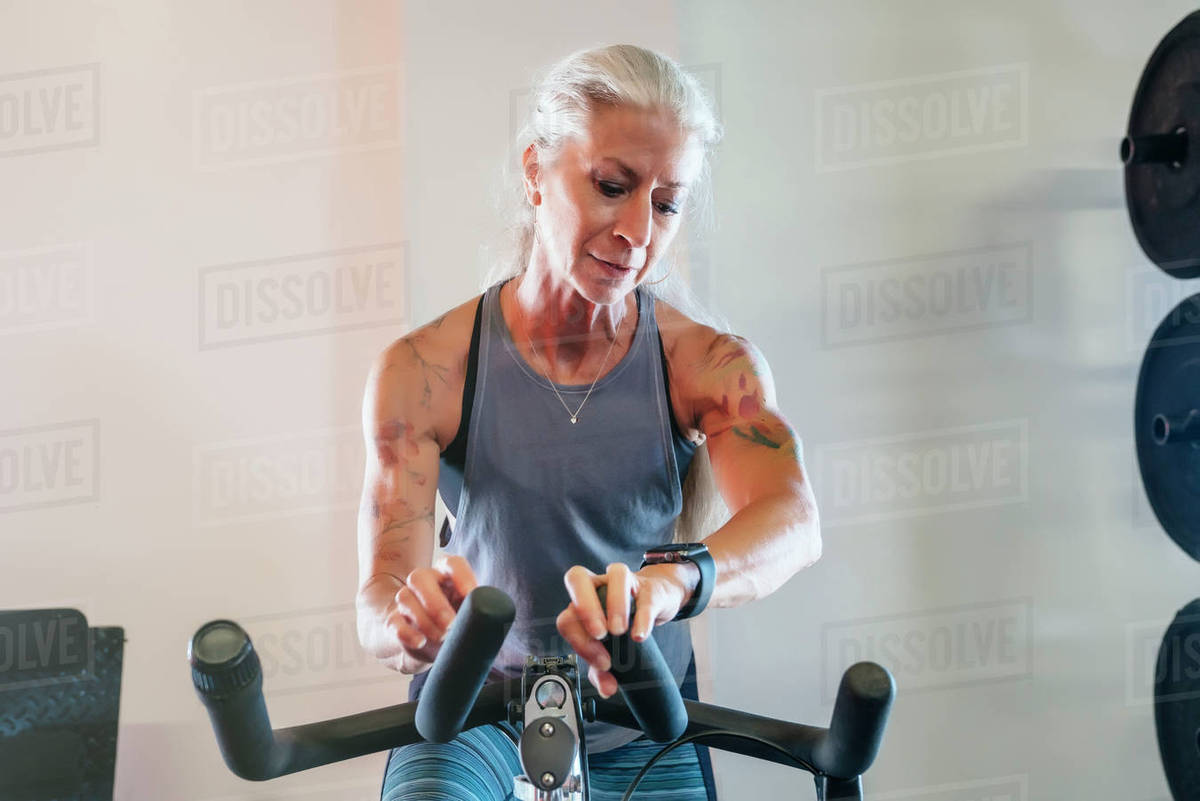 Woman riding stationary bicycle checking smart watch - Royalty-free ...