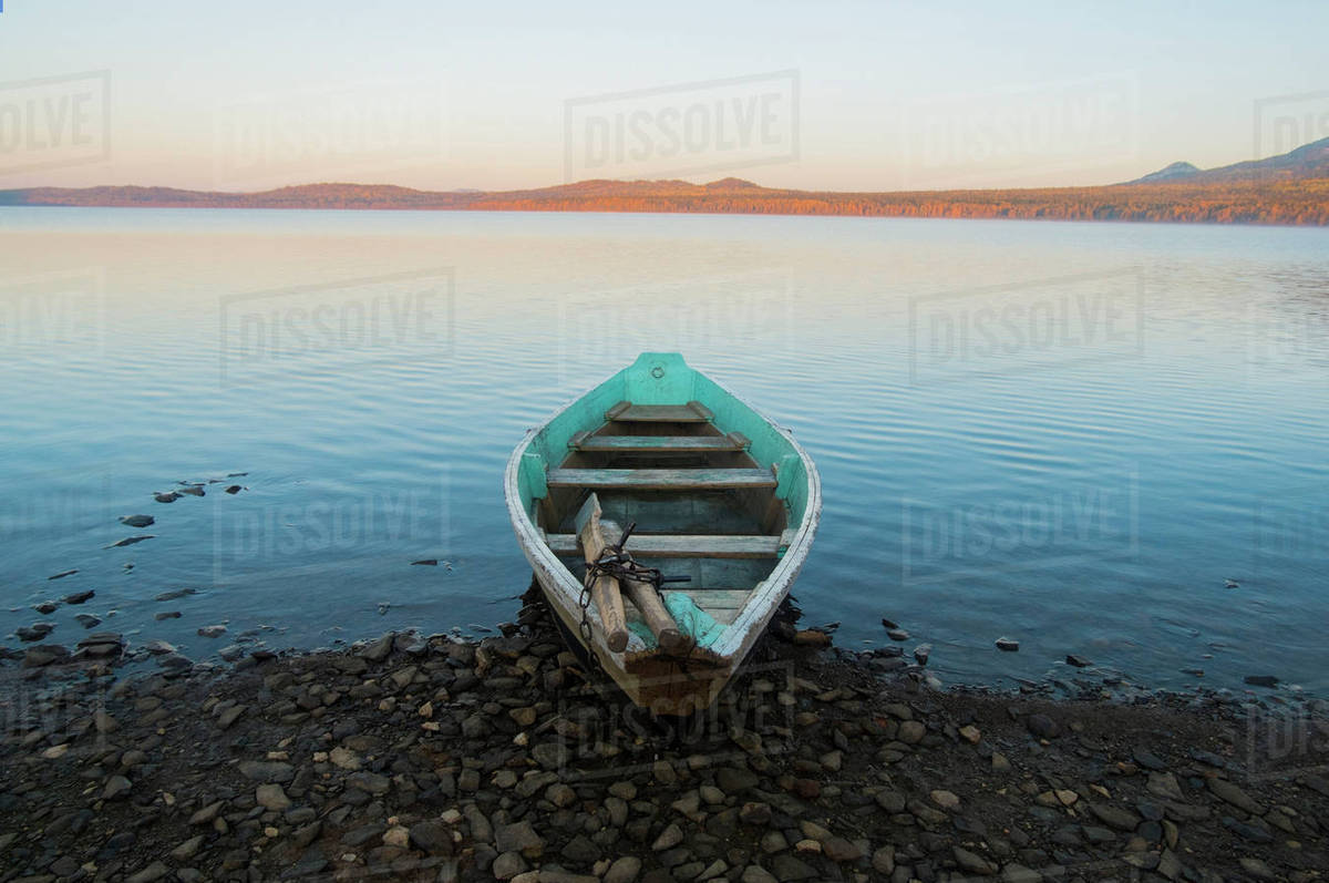 Empty rowboat on rocky shore of lake at sunset - Royalty-free Stock ...