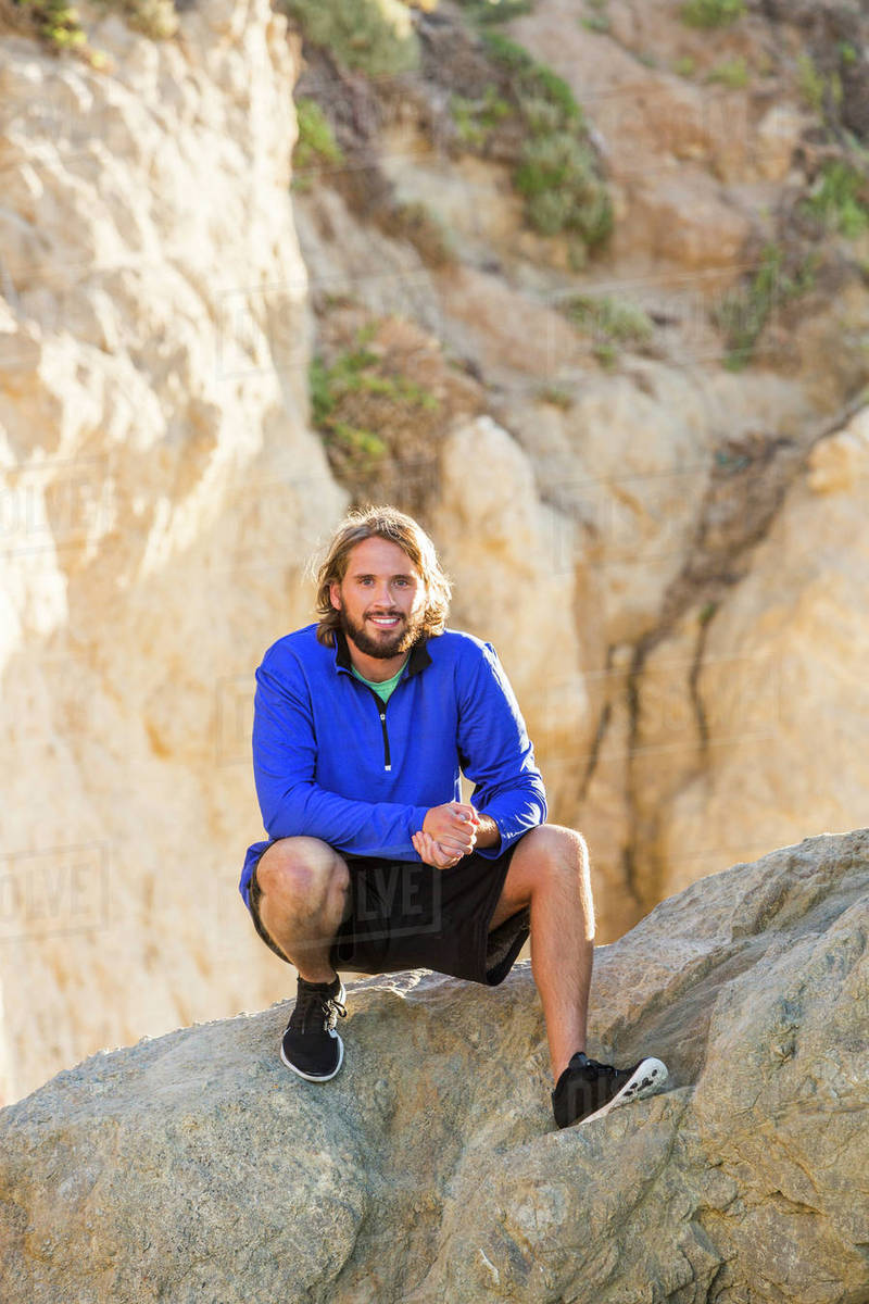Caucasian man crouching on rock formation - Royalty-free Stock Photo ...
