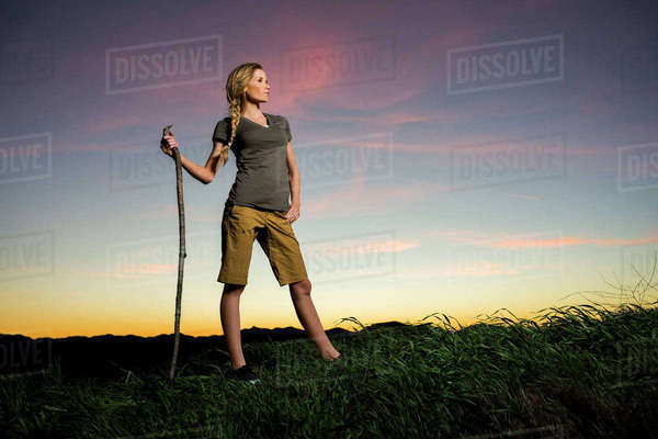 Caucasian woman holding walking stick at sunset - Stock Photo - Dissolve