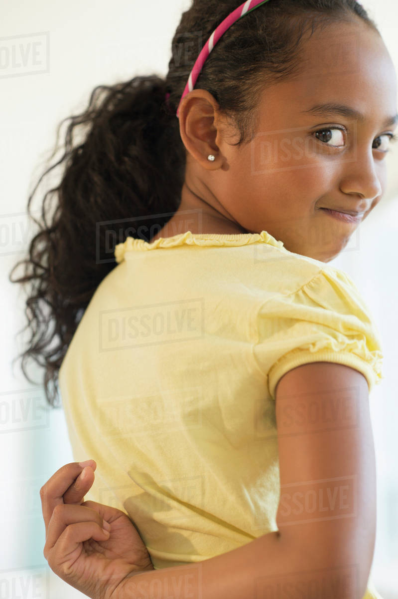 Mixed race girl crossing fingers behind her back - Stock Photo - Dissolve