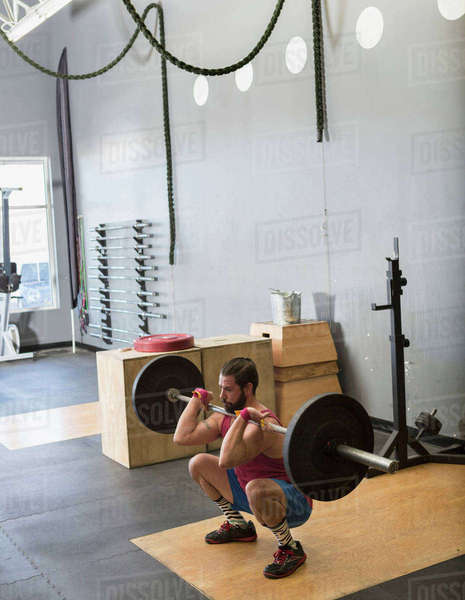 Mixed Race man lifting barbell in gymnasium - Stock Photo - Dissolve