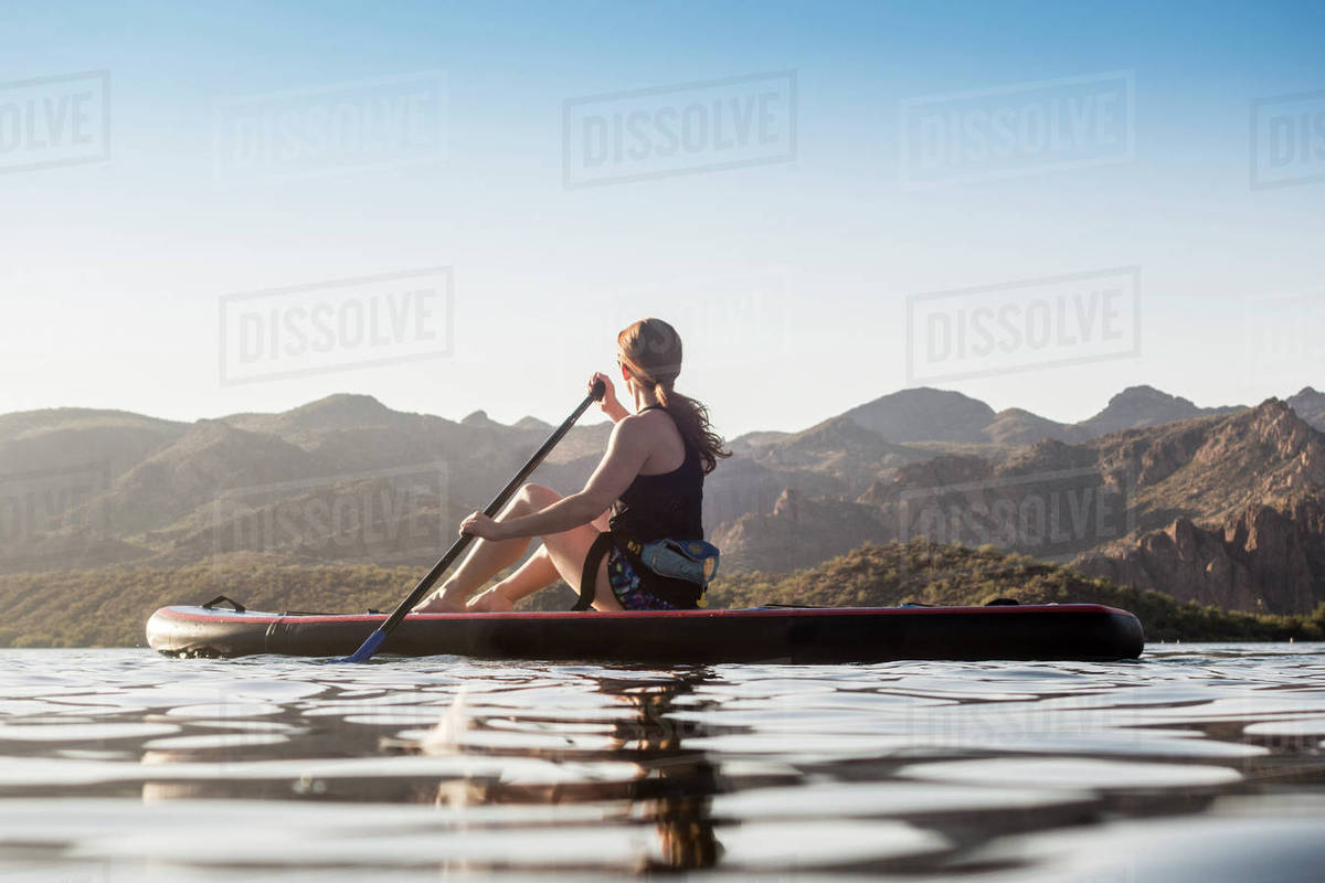 Woman sitting on paddleboard in river - Stock Photo - Dissolve