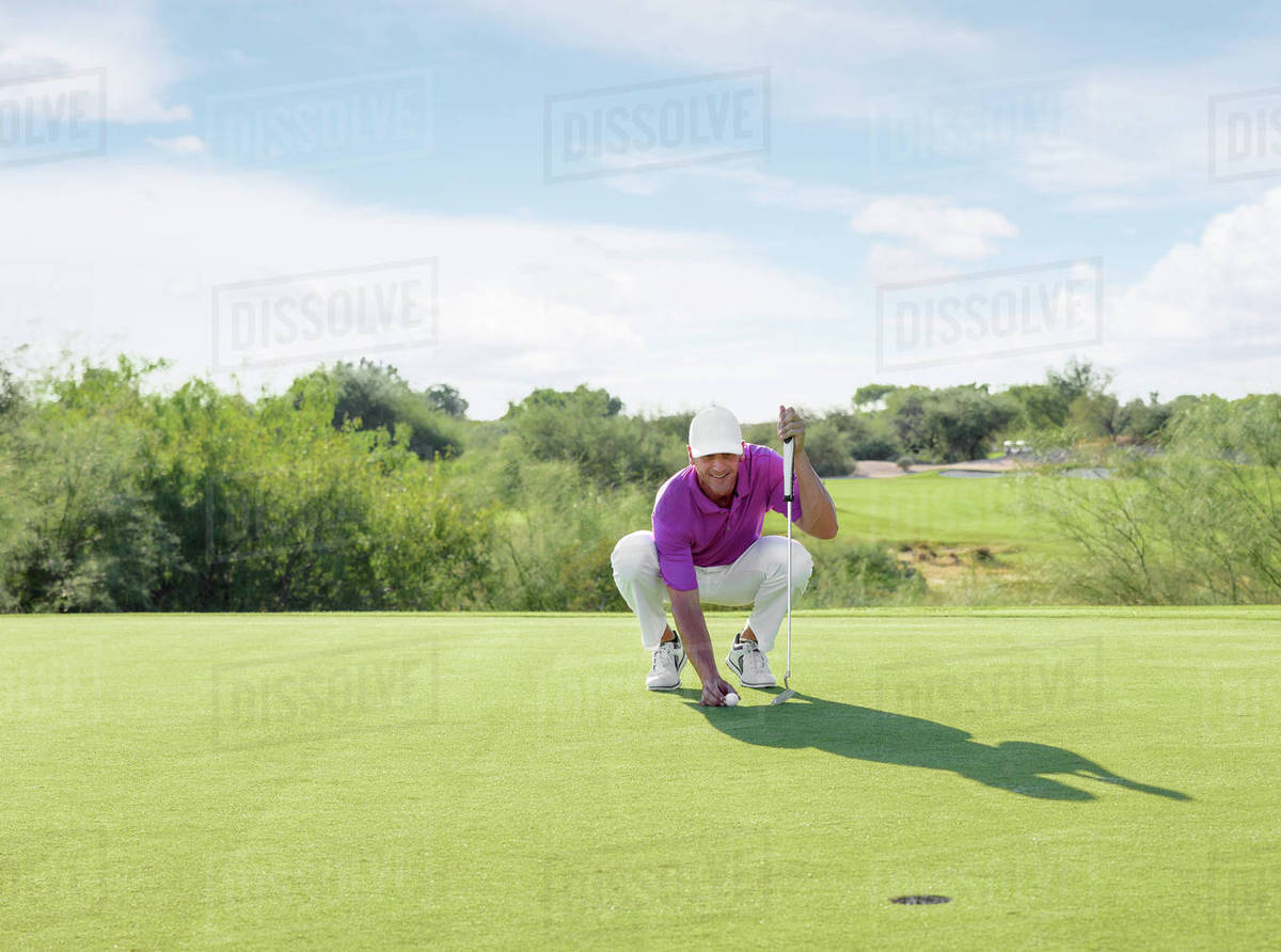 Hispanic golfer crouching on golf course - Stock Photo - Dissolve