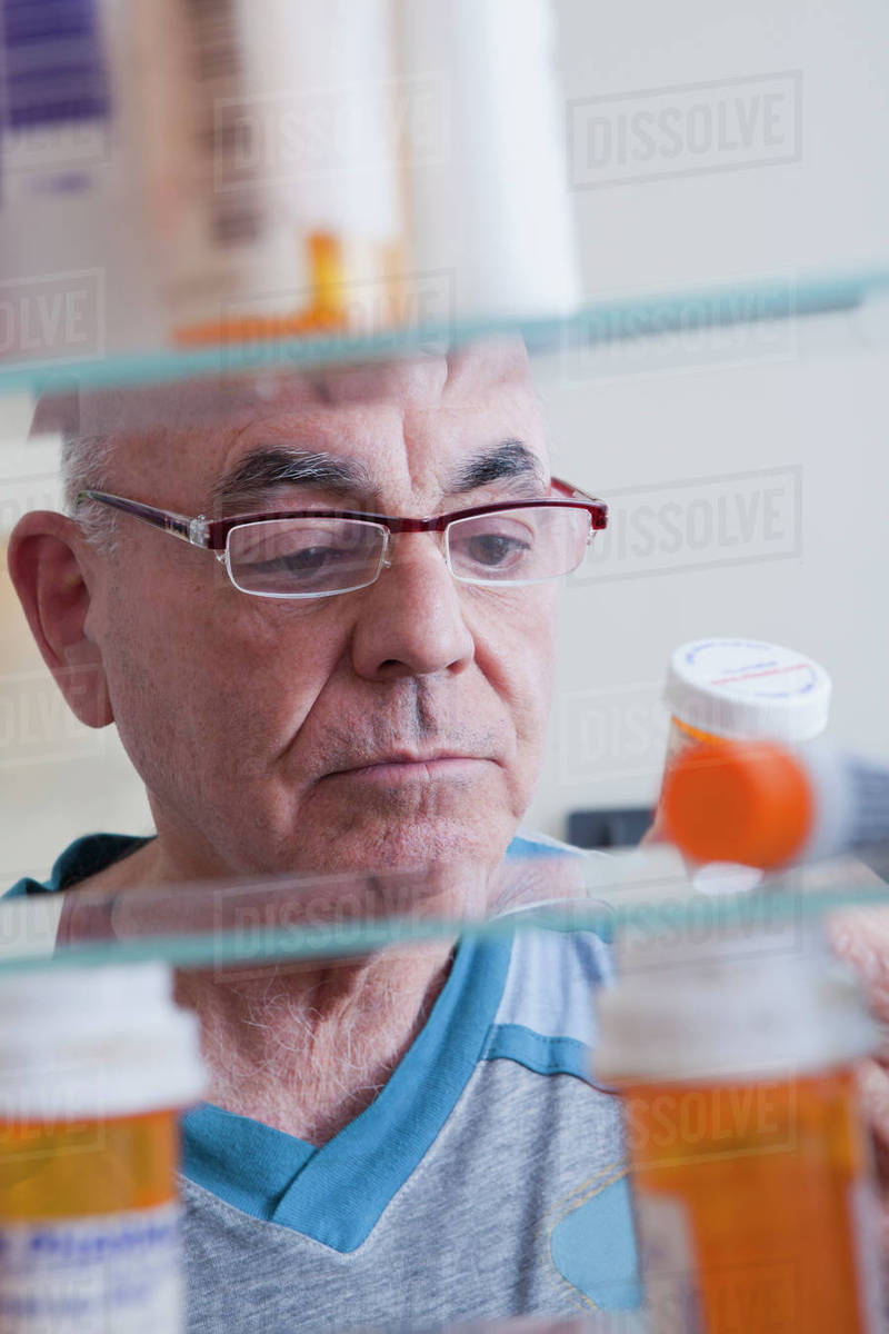 Hispanic man examining pill bottle from medicine cabinet - Royalty-free ...