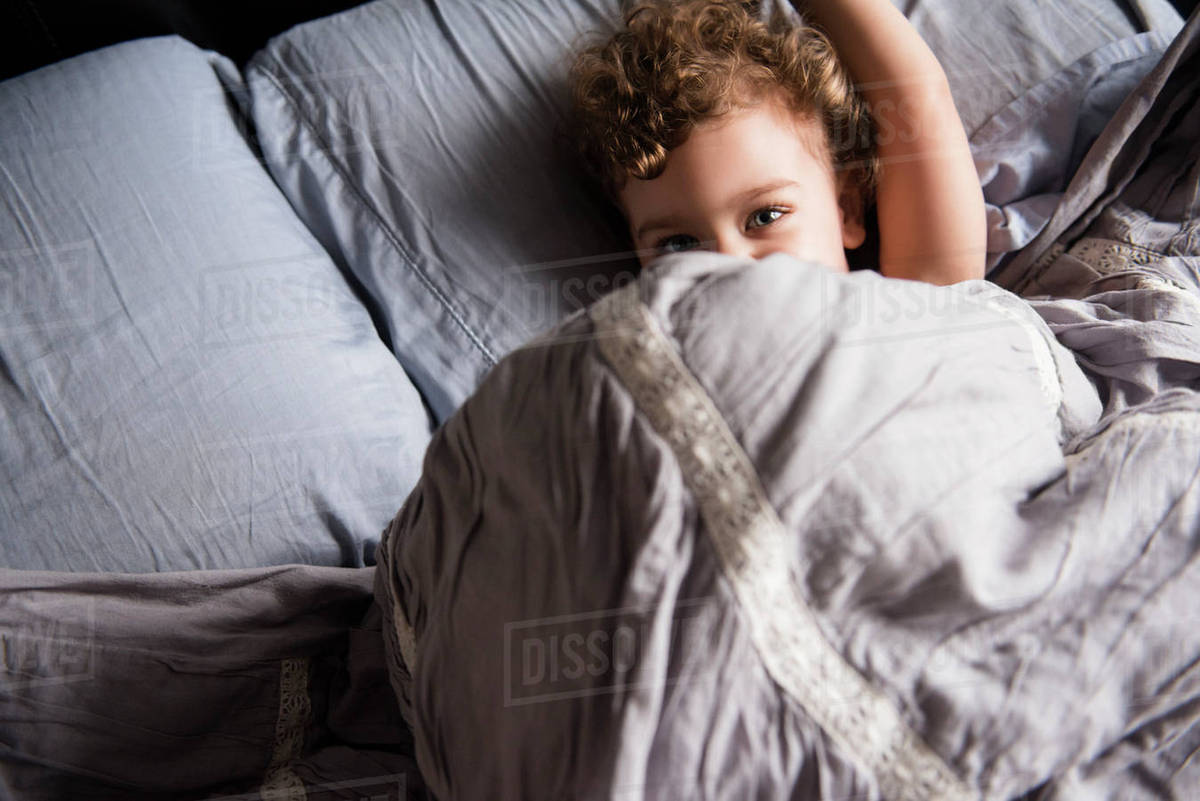 Caucasian boy hiding under blanket in bed - Stock Photo - Dissolve