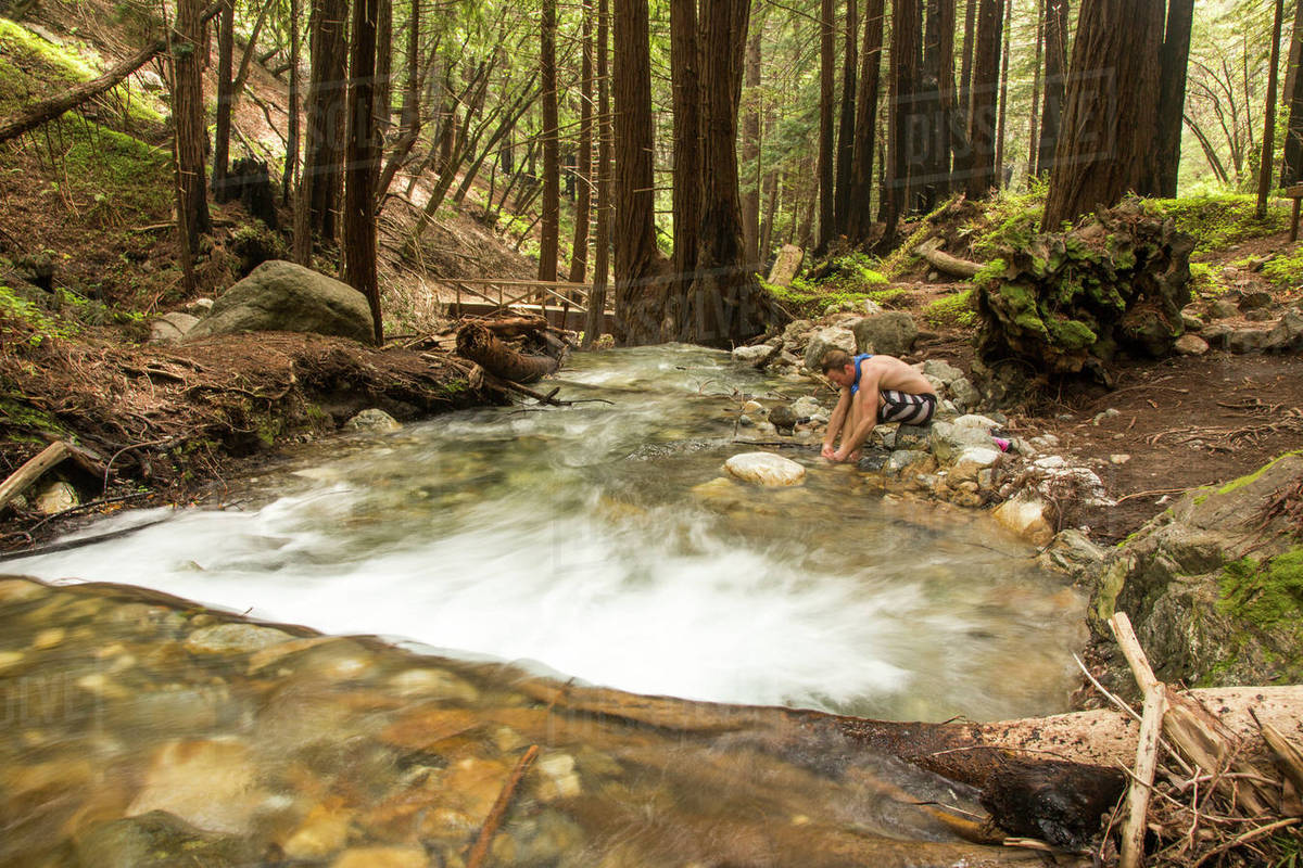 Caucasian man washing foot in forest river - Stock Photo - Dissolve