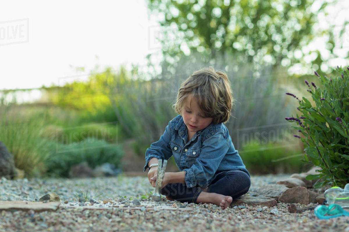 Caucasian boy sitting on ground smashing rocks with hammer - Royalty ...