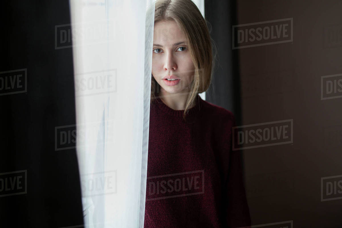 Serious Caucasian woman standing near curtain at window - Stock Photo ...