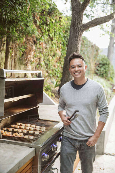 Portrait of smiling Chinese man cooking on grille - Stock Photo - Dissolve