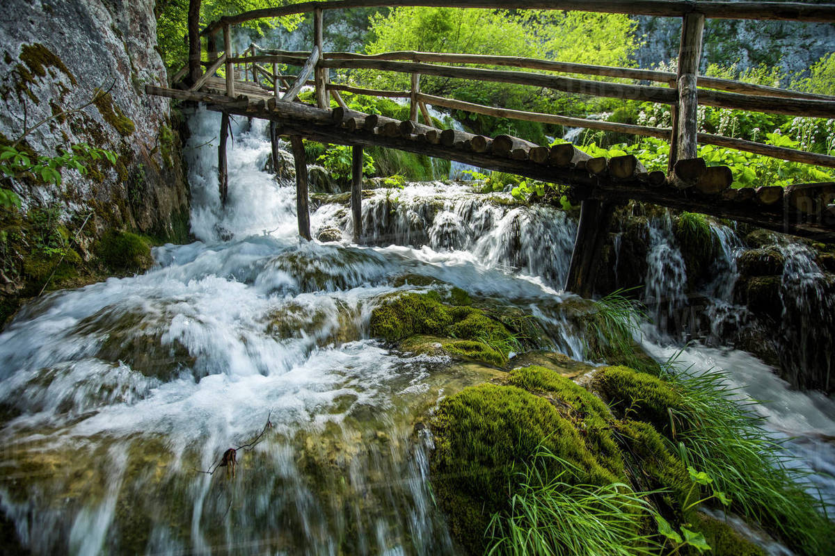 Wooden footbridge over waterfall - Stock Photo - Dissolve