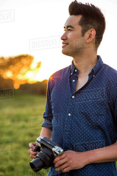 Smiling Chinese man holding camera in field - Royalty-free Stock Photo ...