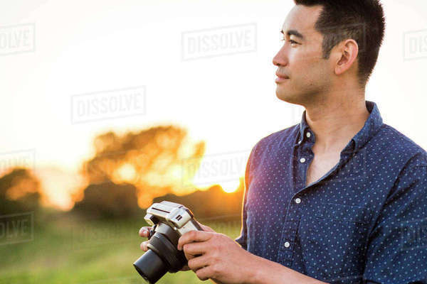 Smiling Chinese man holding camera in field - Royalty-free Stock Photo ...