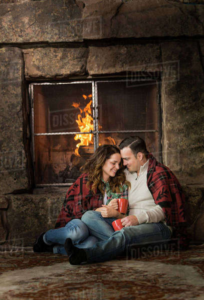 Smiling Caucasian couple cuddling on floor near fireplace - Royalty ...