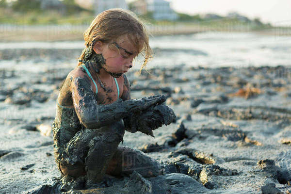Caucasian girl covered in mud playing on beach - Stock Photo - Dissolve