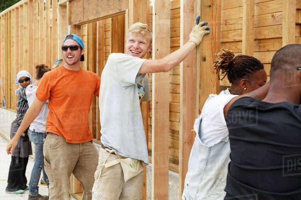 Smiling volunteers holding framed wall at construction site - Royalty ...