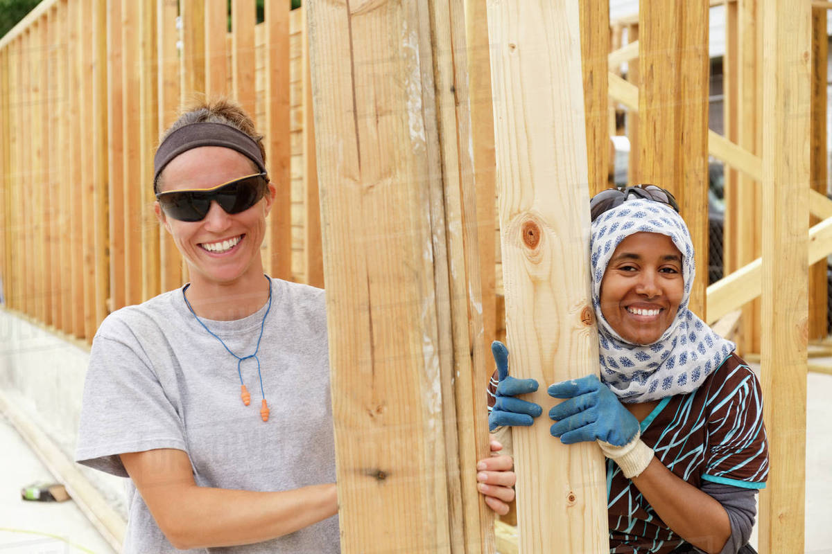 Smiling volunteers holding lumber at construction site - Royalty-free ...