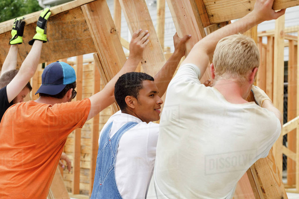 Volunteers lifting framed wall at construction site - Royalty-free ...