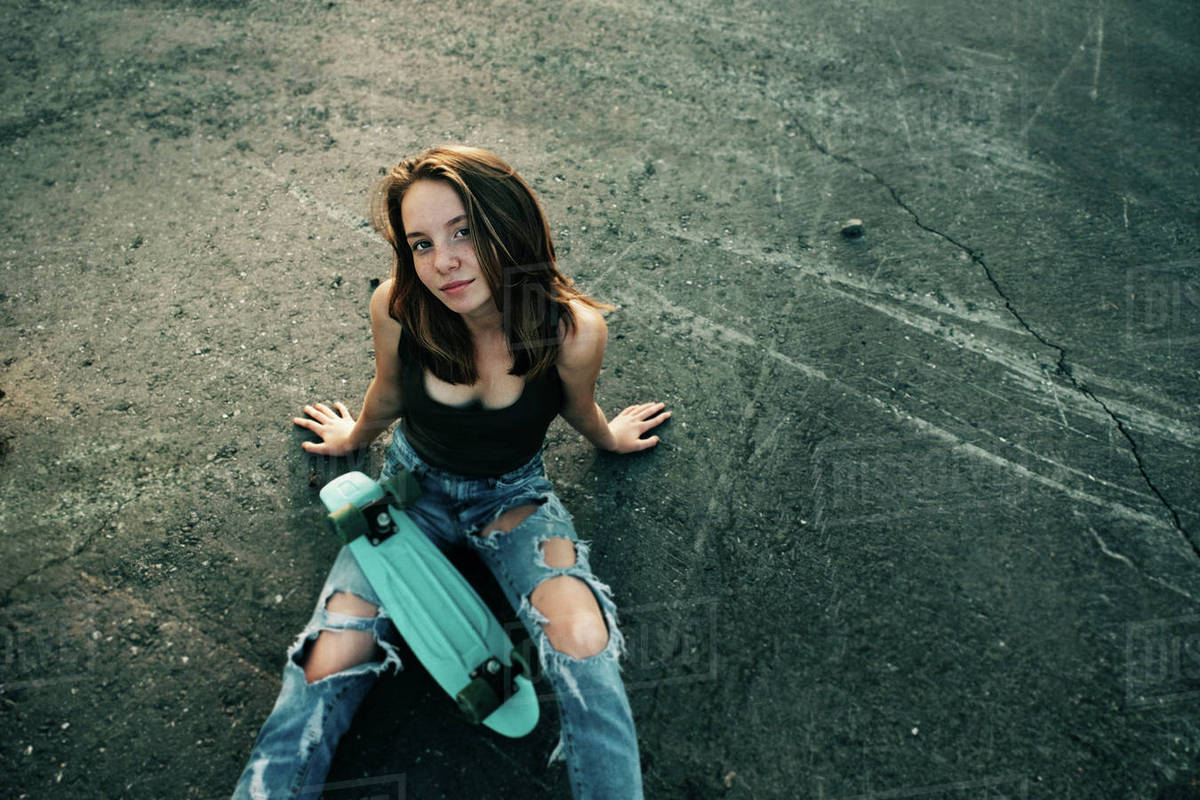 Caucasian teenage girl sitting on pavement with skateboard - Stock ...