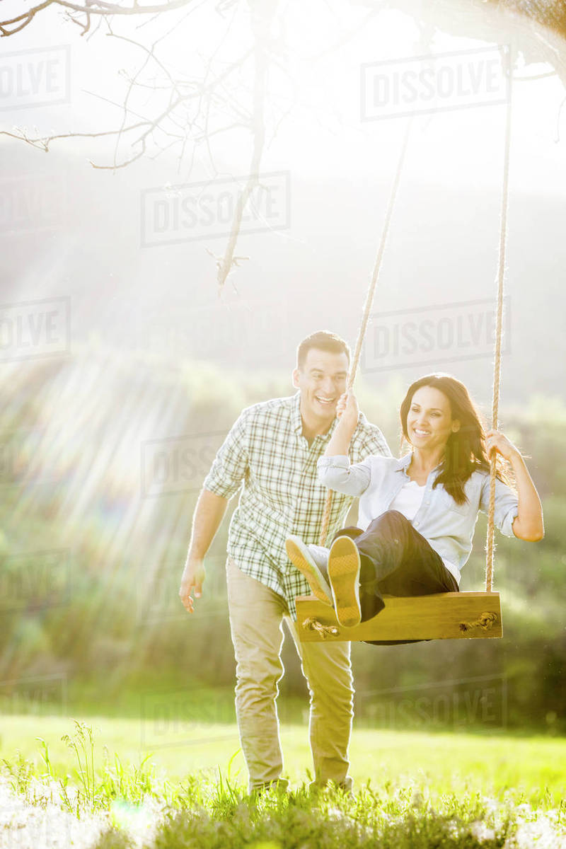 Man pushing woman swinging on tree swing - Royalty-free Stock Photo ...