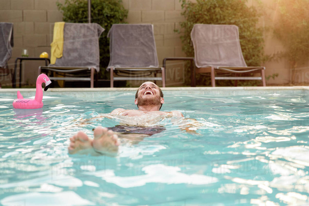 Smiling Caucasian man floating in swimming pool - Stock Photo - Dissolve