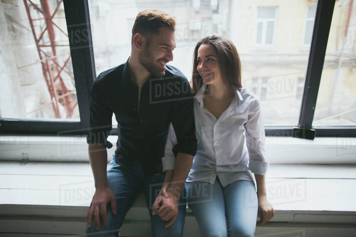 Caucasian couple sitting on window sill holding hands - Stock Photo ...