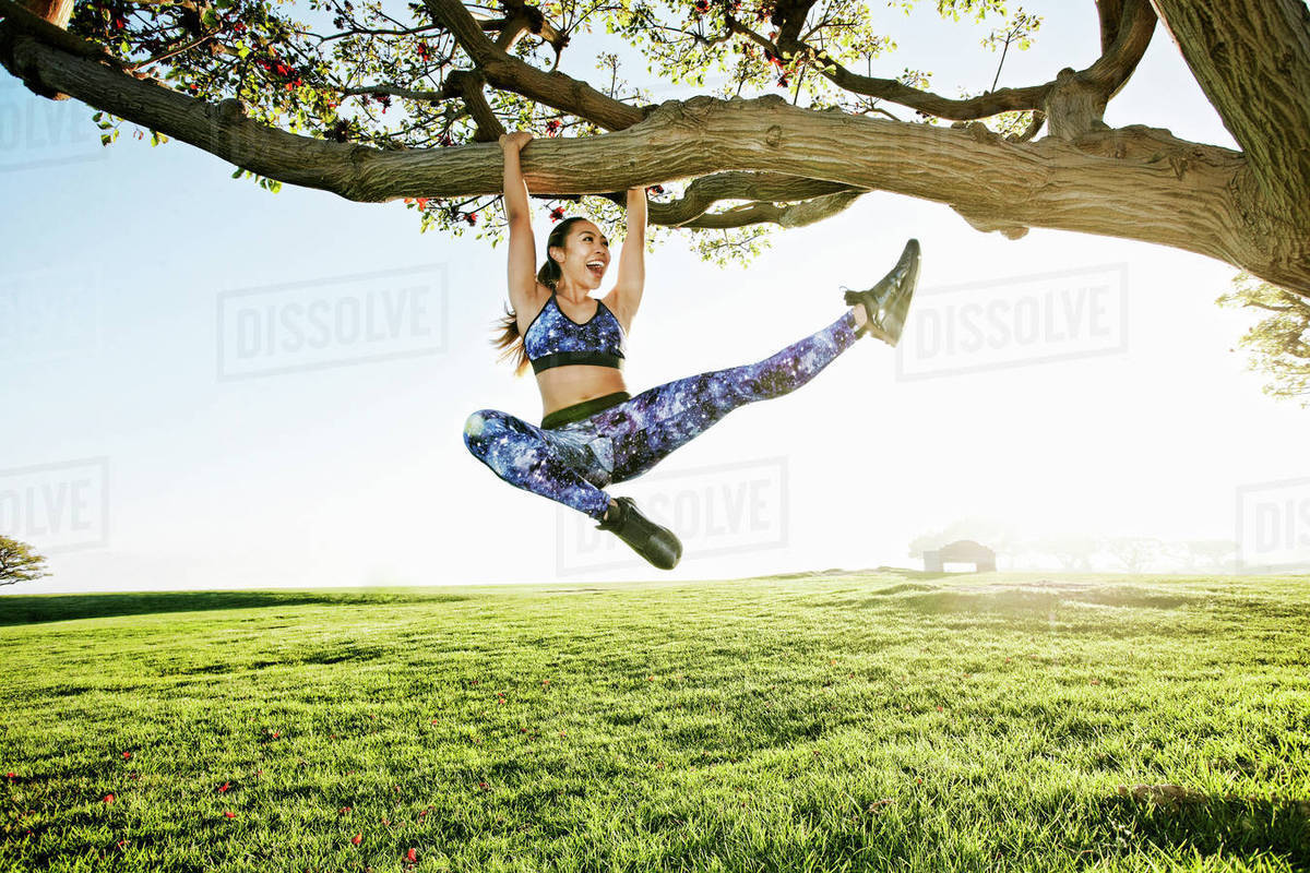 Happy mixed race woman hanging on tree branch - Stock Photo - Dissolve