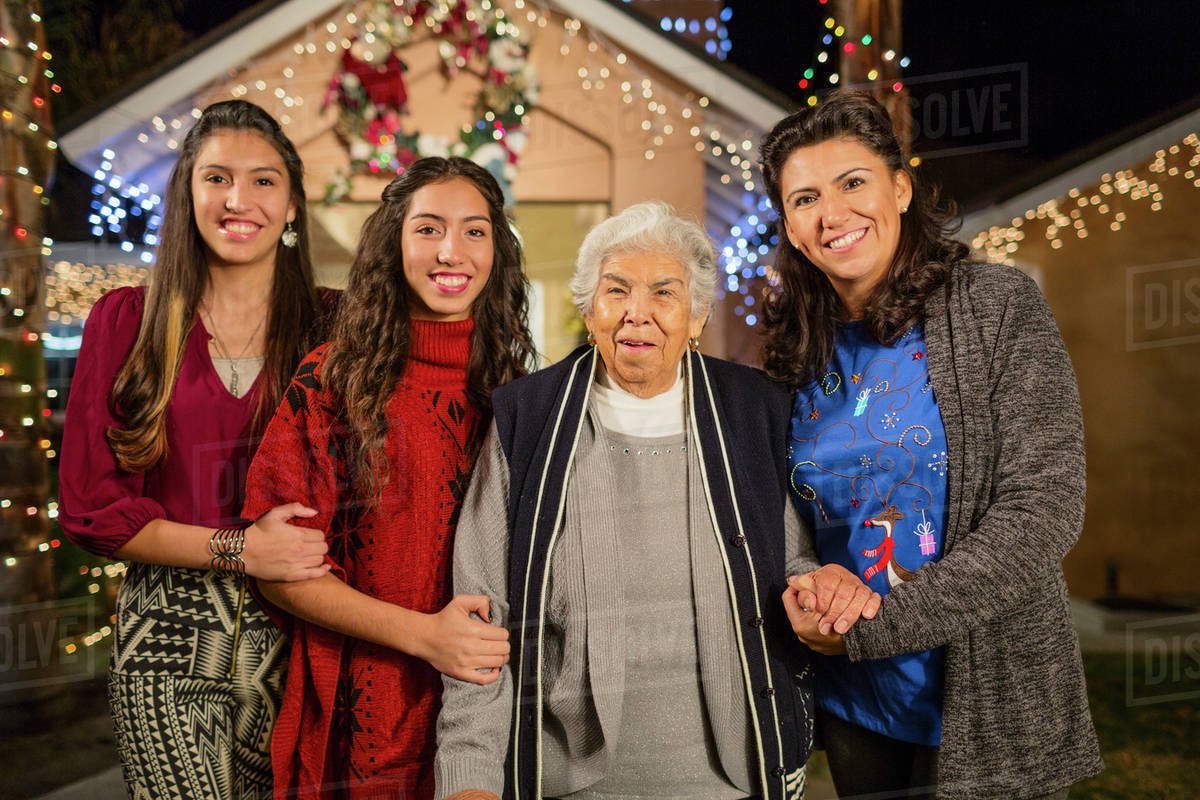 Three generations of Hispanic women smiling outside house decorated ...