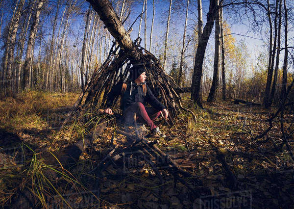 Man sitting in wooden shelter in forest - Stock Photo - Dissolve